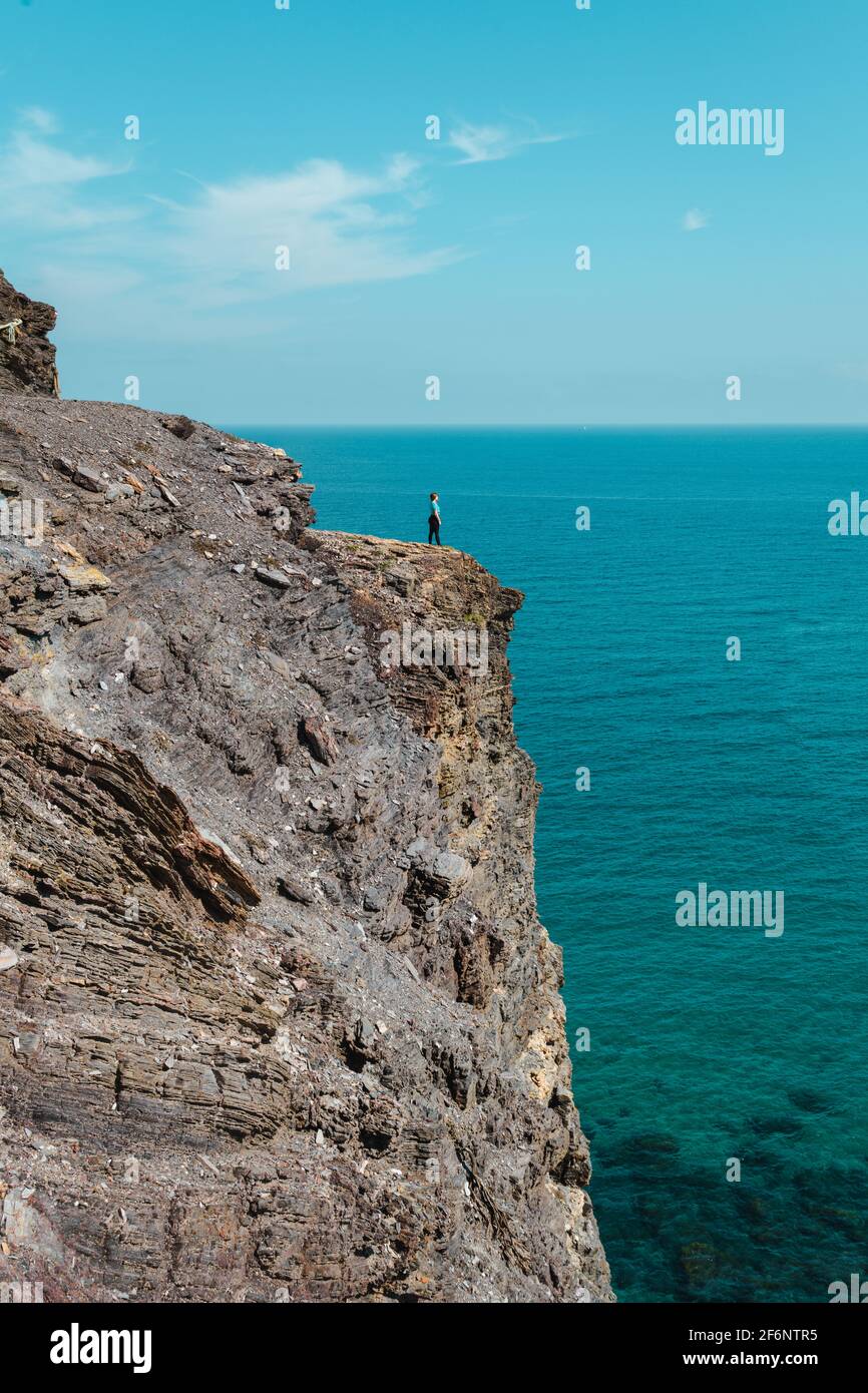 Blonde young woman on top of a cliff looking at the blue mediterranean ...