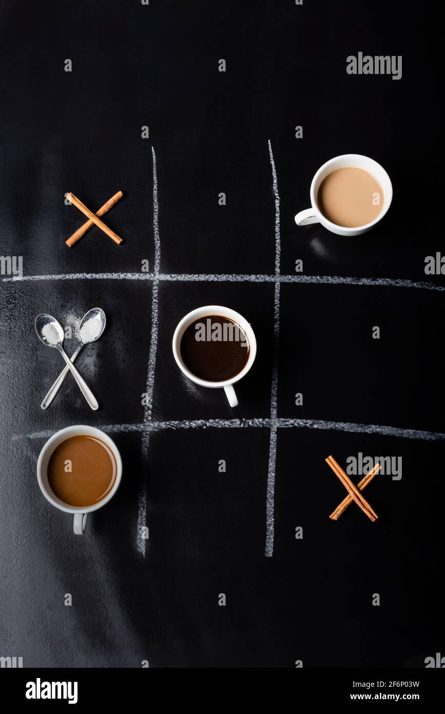 top view of tic tac toe game with spoons, cinnamon sticks and cups of ...