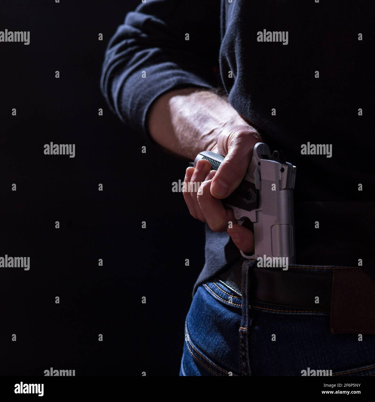 Male hand taking a gun from his belt behind the back, on black ...