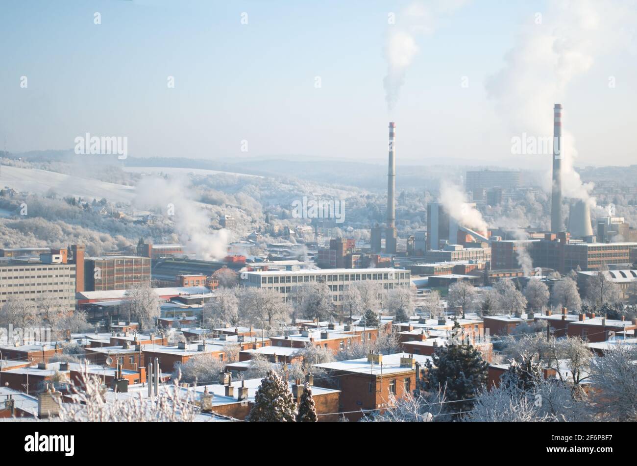 A landscape of a factory with smokestacks covered in late winter snow ...