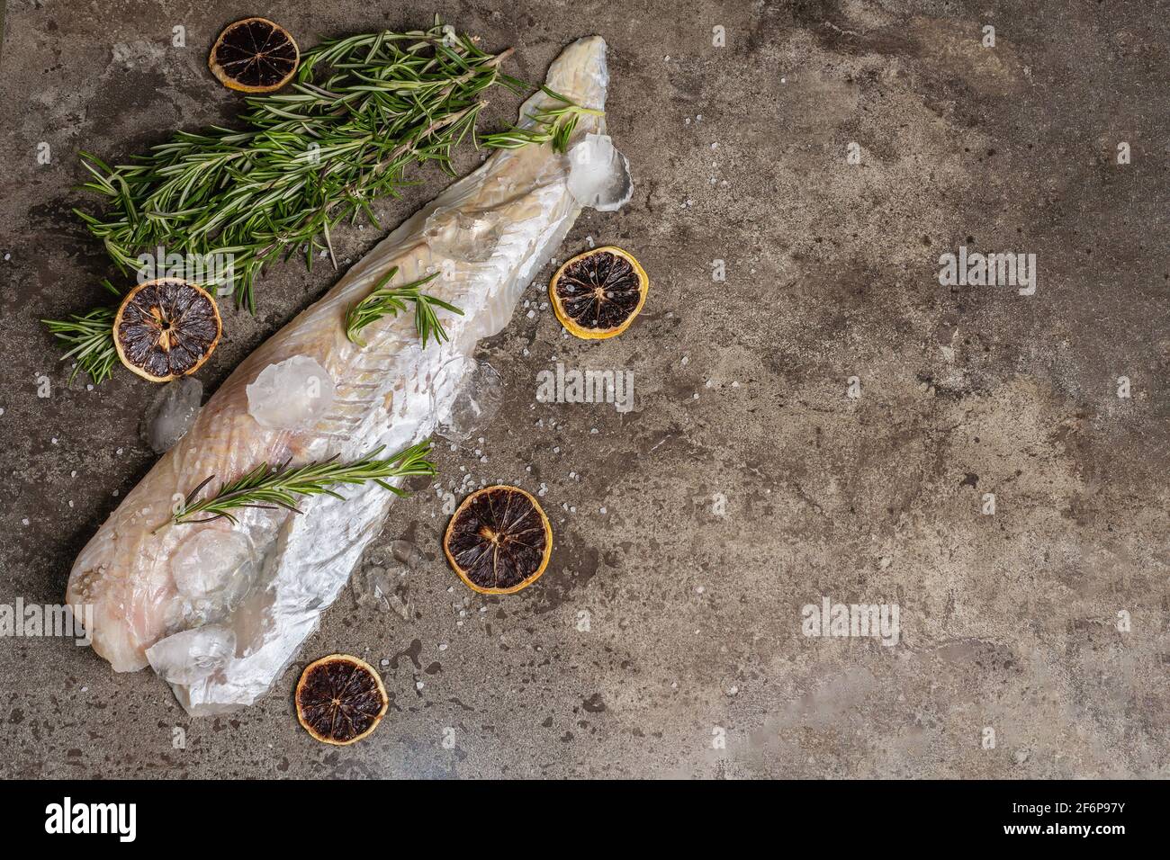 Raw frozen hake fillet with ice, fresh rosemary, and dry lemon slices ...