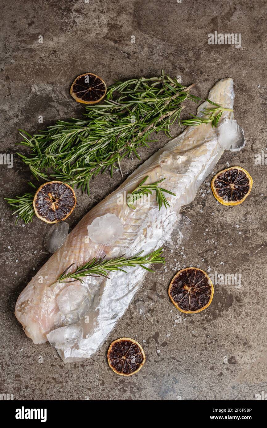 Raw frozen hake fillet with ice, fresh rosemary, and dry lemon slices ...