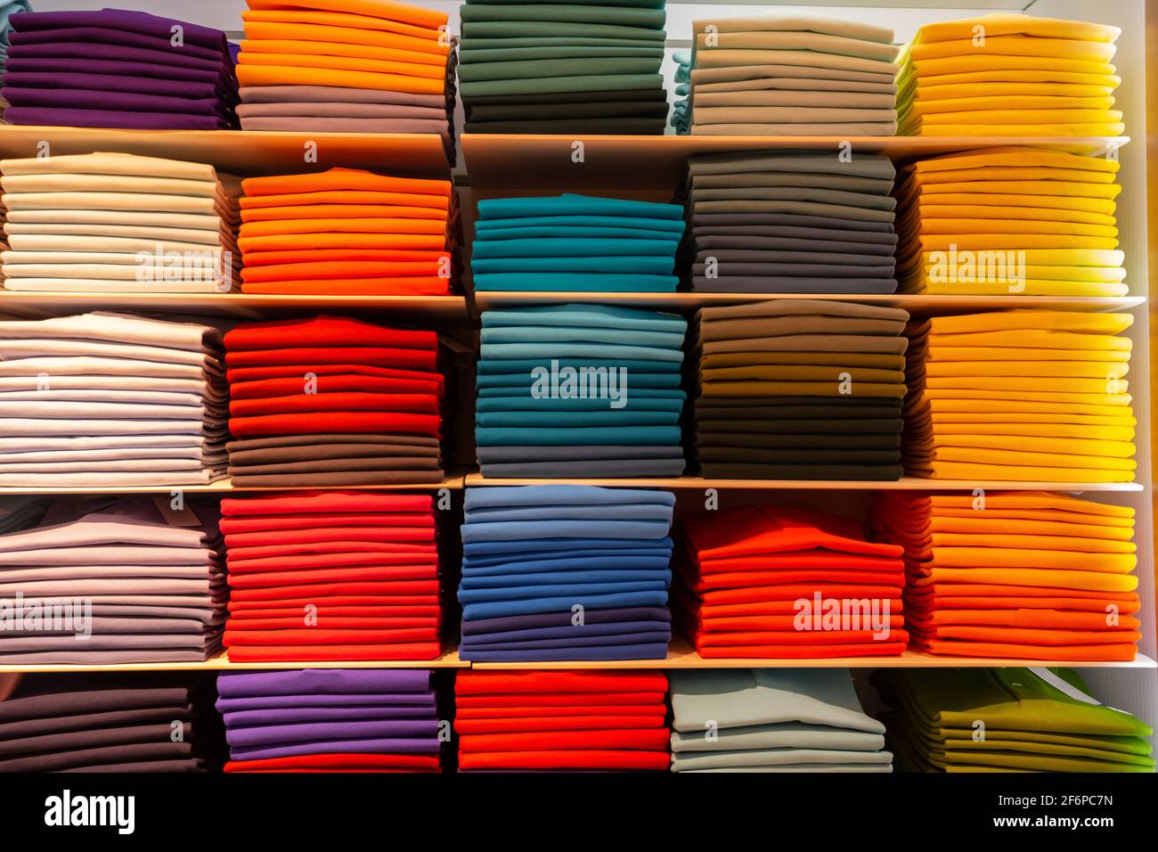 Multicolored clothes folded in a shelve and organized by colour ranges ...