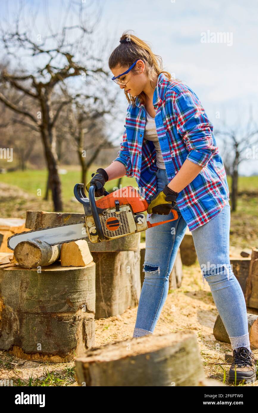 Young Woman using chainsaw to cut a log for firewood Stock Photo - Alamy