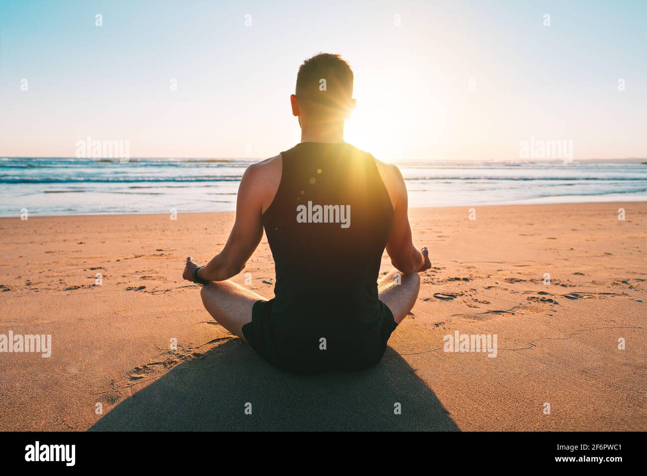 Healthy man practicing yoga and meditates on the beach at sunset or ...