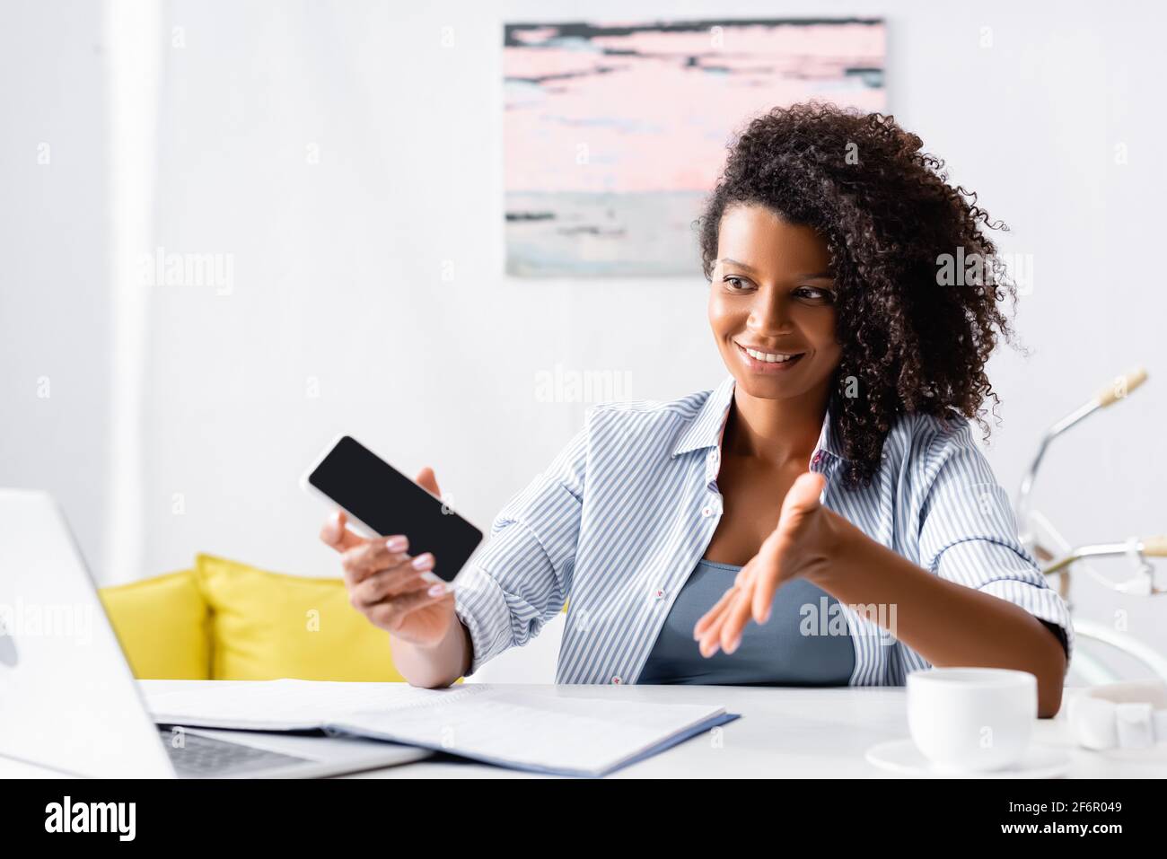Cheerful african american freelancer with smartphone pointing at laptop ...