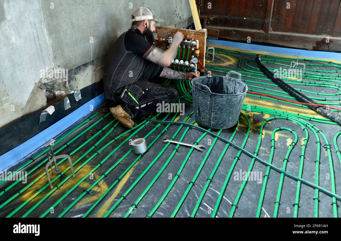 Workman setting up and testing pipework for underfloor heating system ...