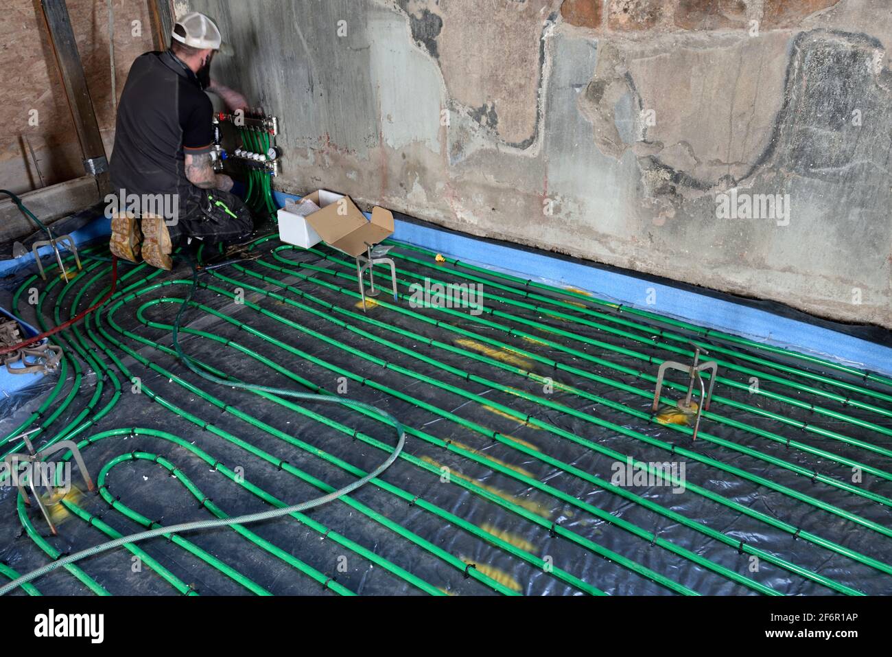 Workman setting up and testing pipework for underfloor heating system ...