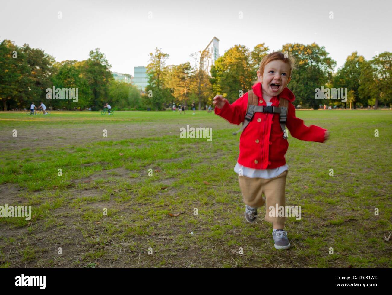 A cute, redhead, baby boy wearing a red jacket running on a lawn in a ...