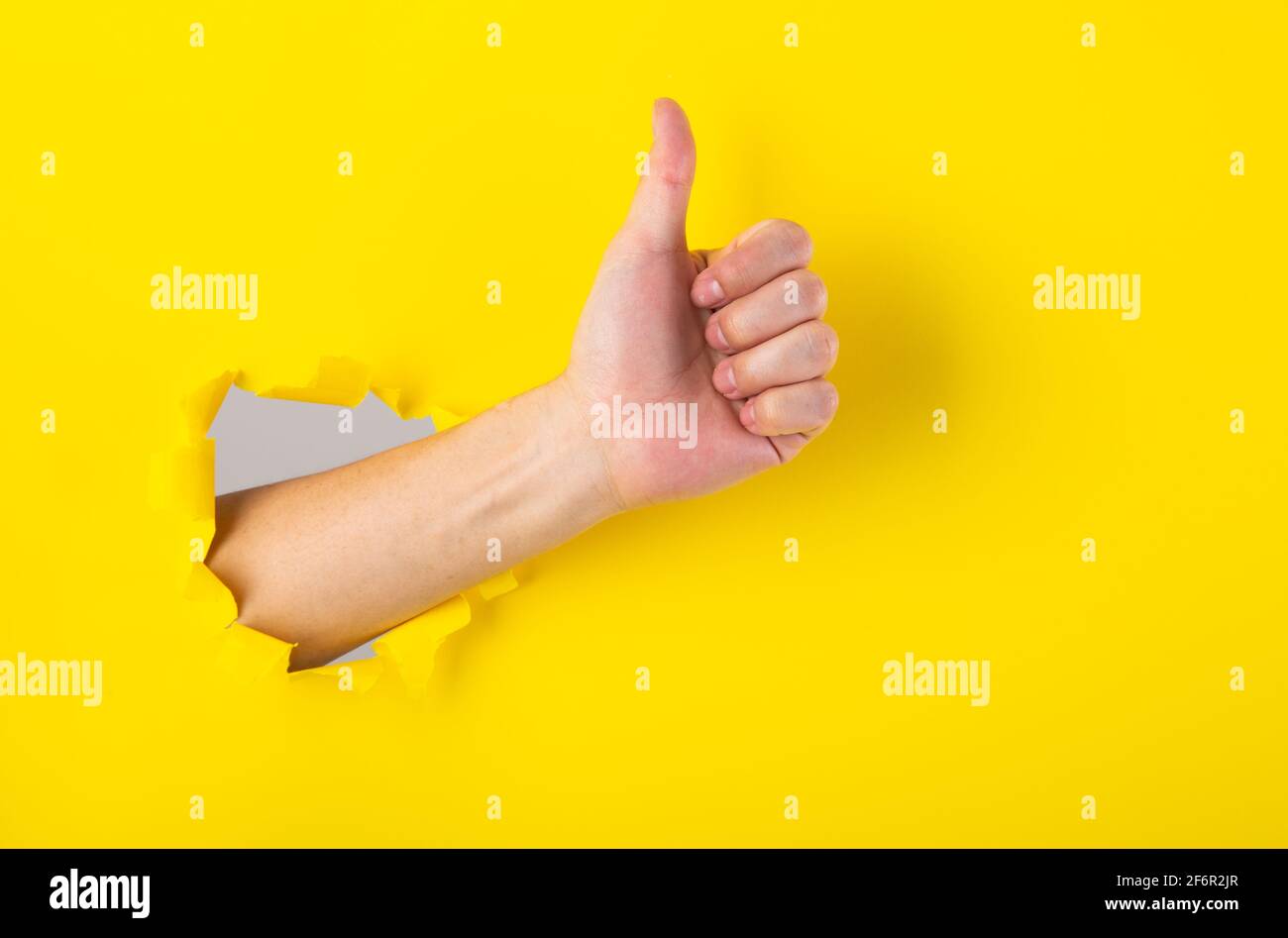 Hand showing a thumb up sign through a ripped hole in yellow paper ...