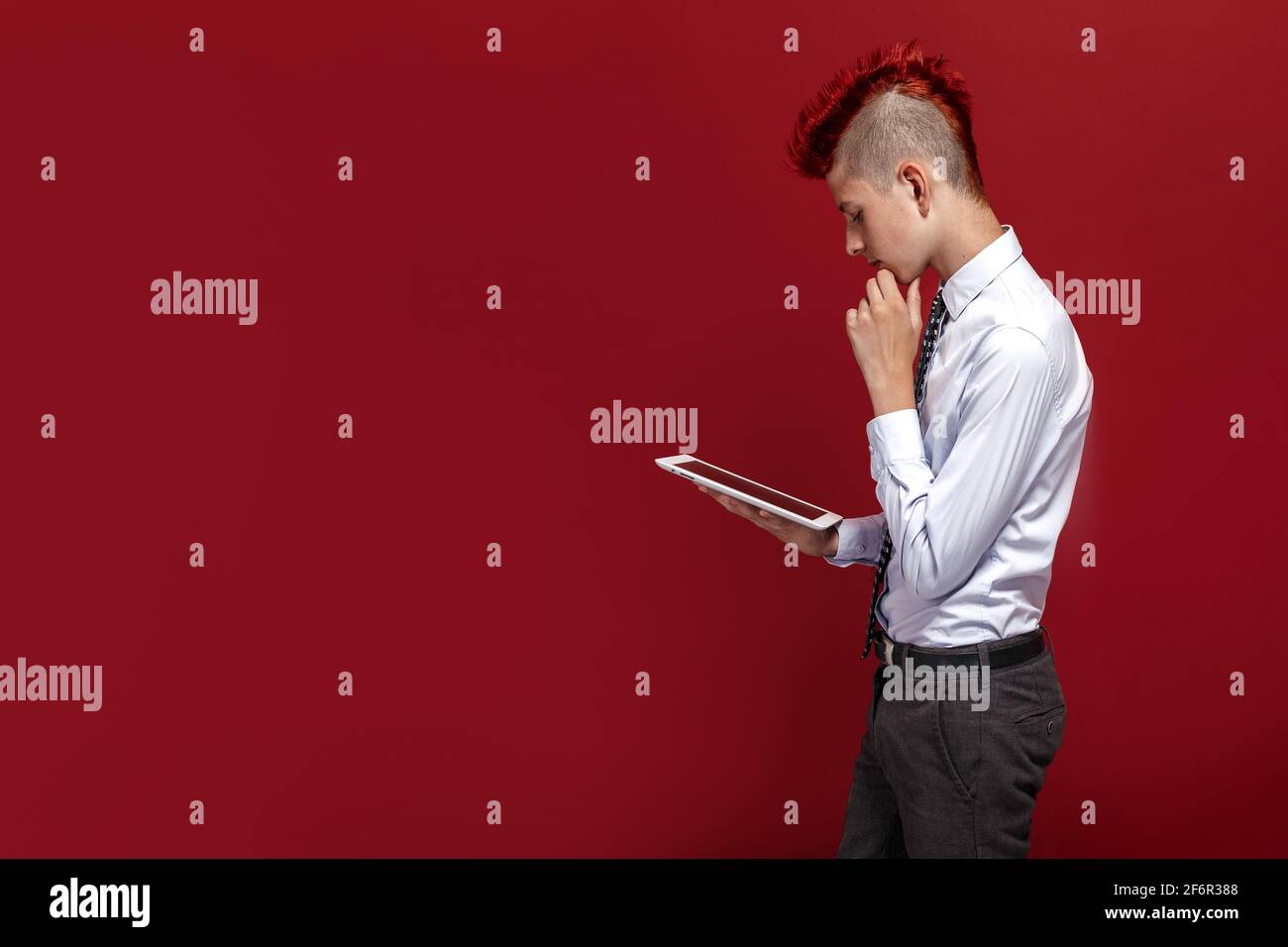 Side view of red-haired teen punk with tablet against of red background ...