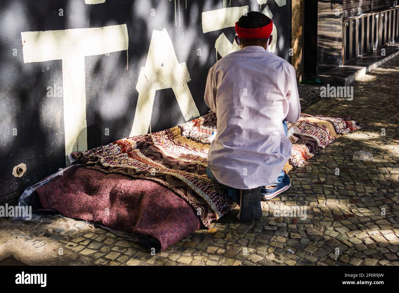 Brazilian homeless man kneeling by his mattress on the sidewalk of a ...