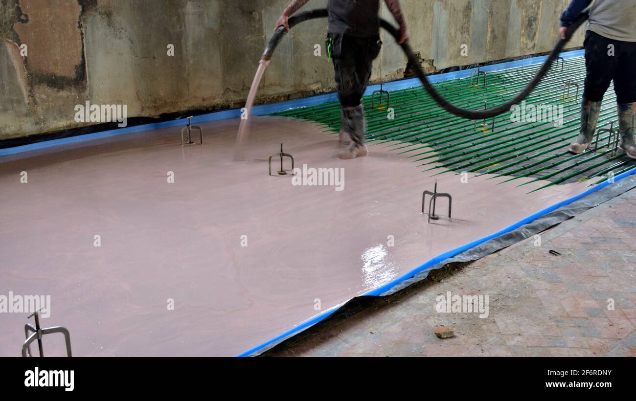 Workman pouring pumped anhydrite self levelling screed over underfloor ...