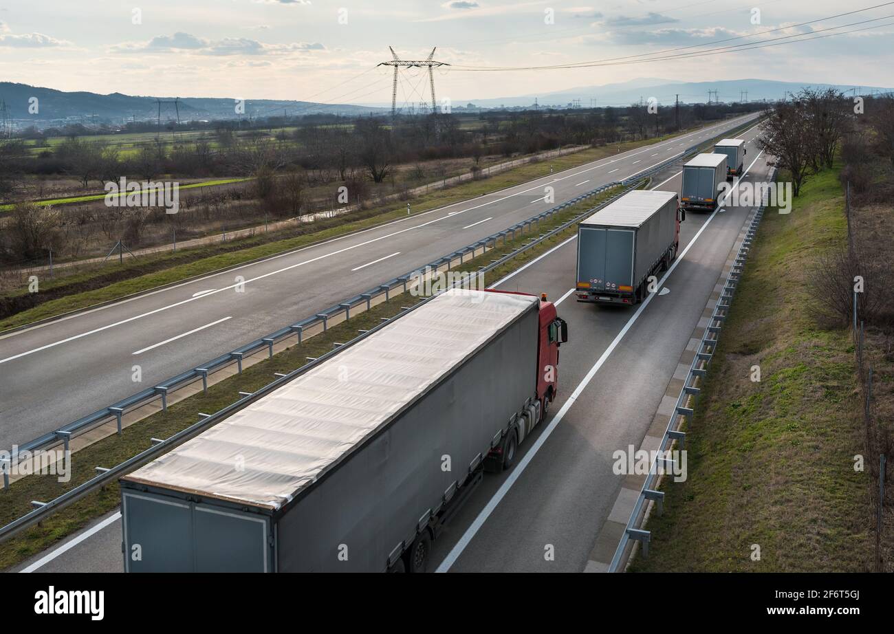 Convoy of Big Transportation trucks departing on a country highway ...