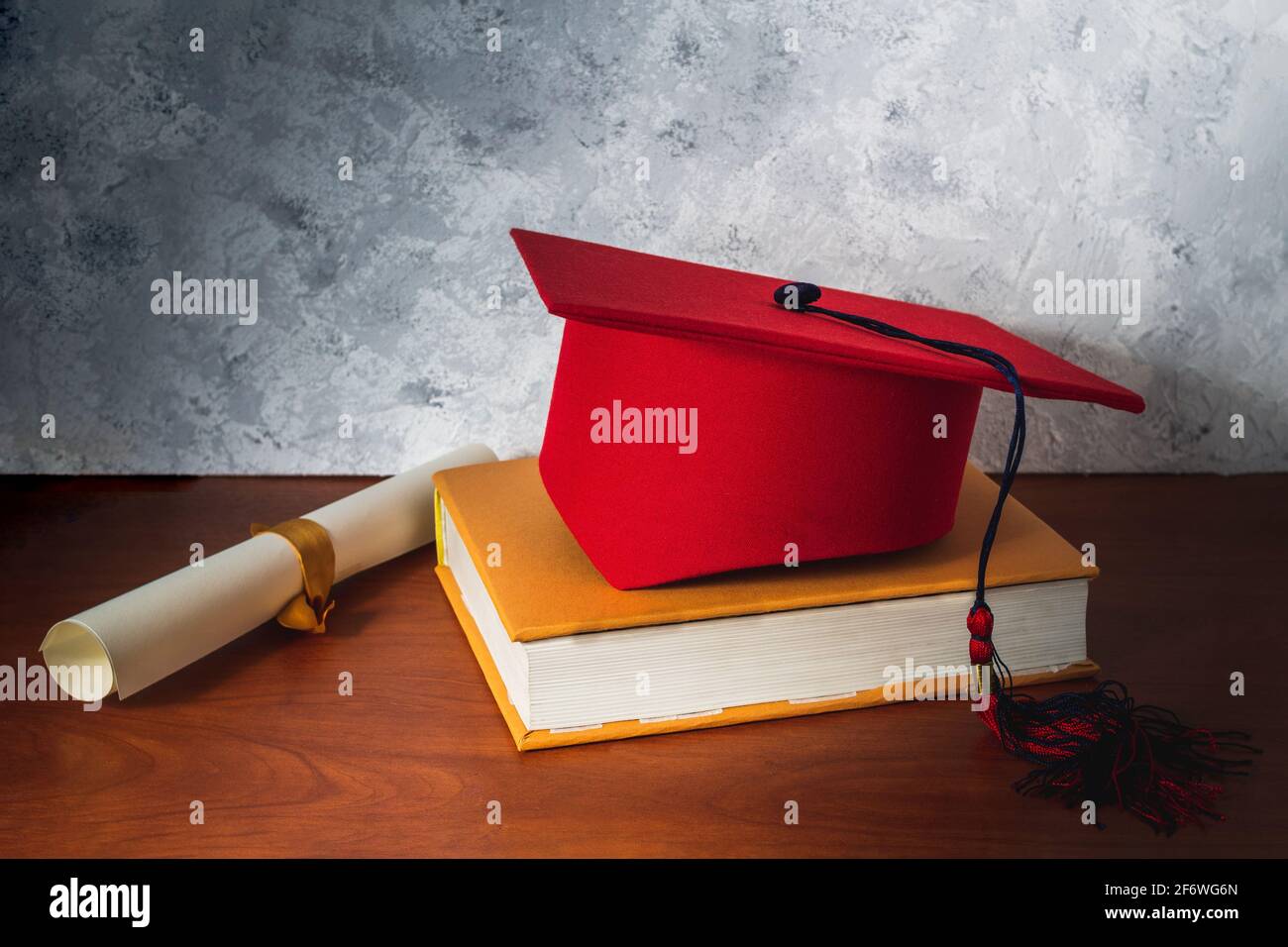 Still life with a red graduation hat on a book next to a diploma on a ...