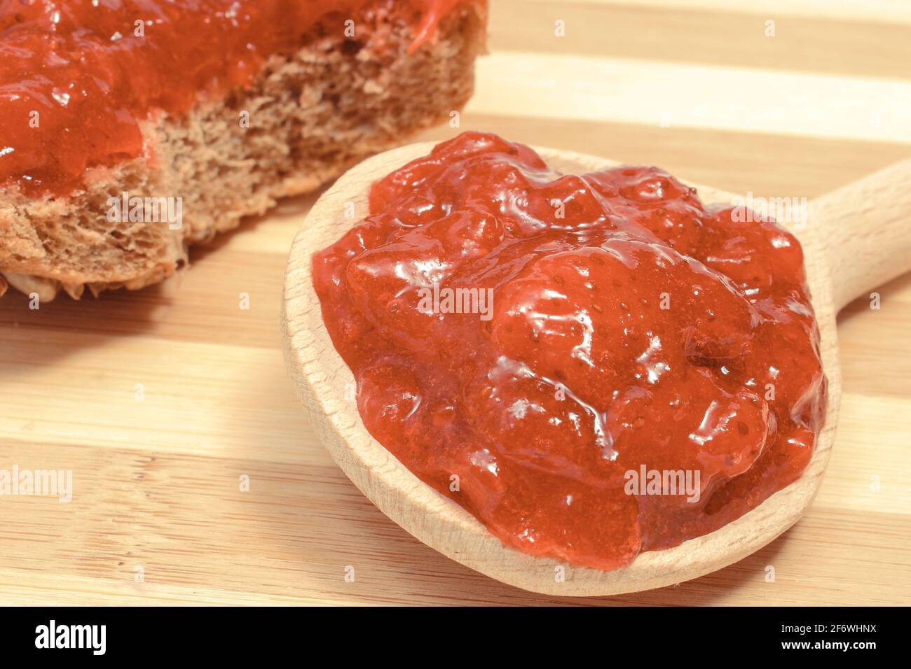 Homemade strawberry jam on wooden spoon and portion of wheat or rye ...