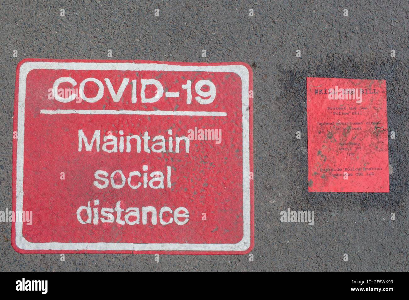 On the footpath is a red Covid-19 social distancing sign next to a red ...