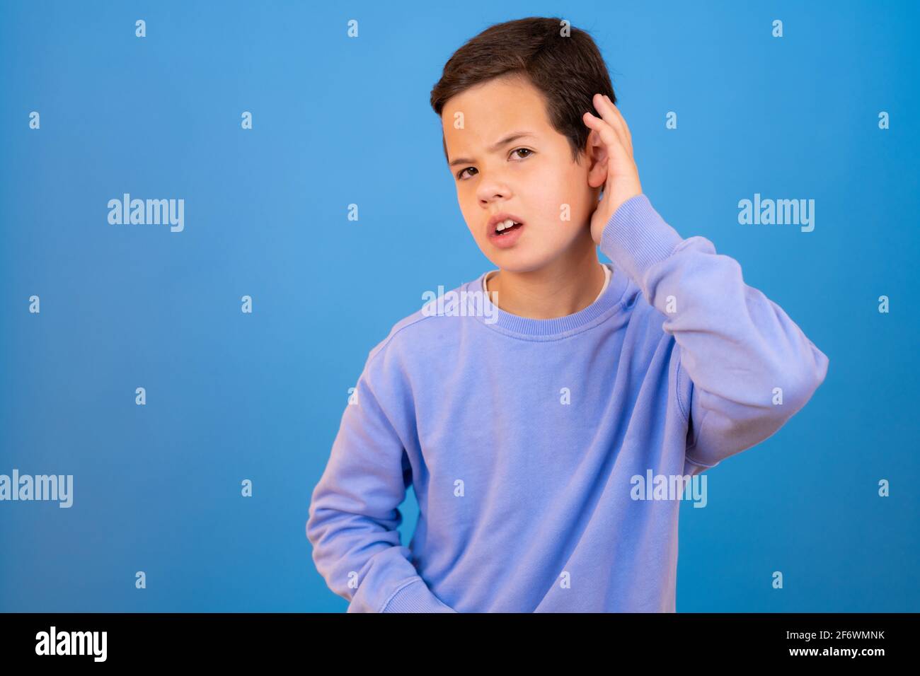 Concentrated young boy making a gesture of trying to hear something ...