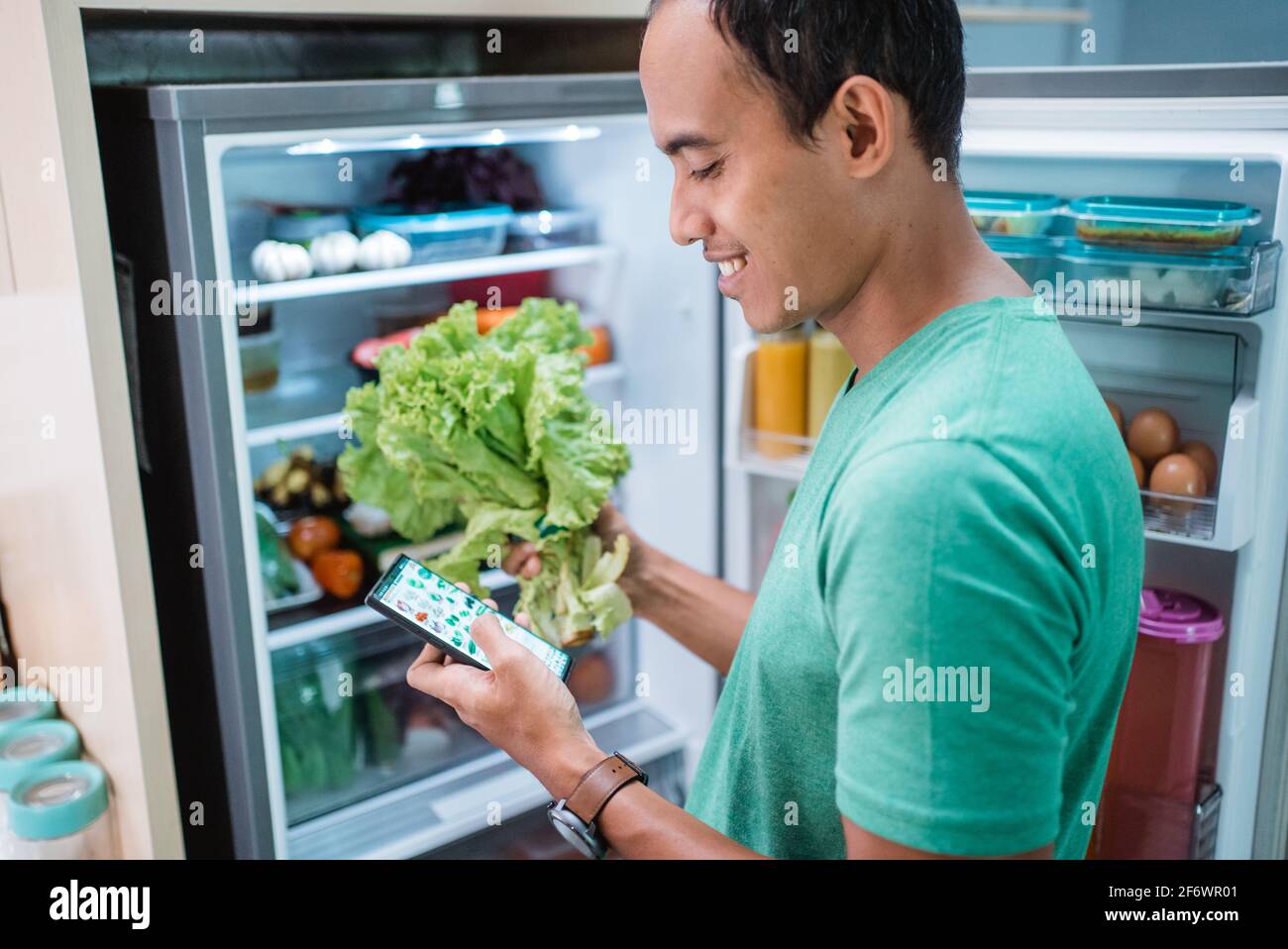 man standing in front of the fridge while holding his mobile phone ...