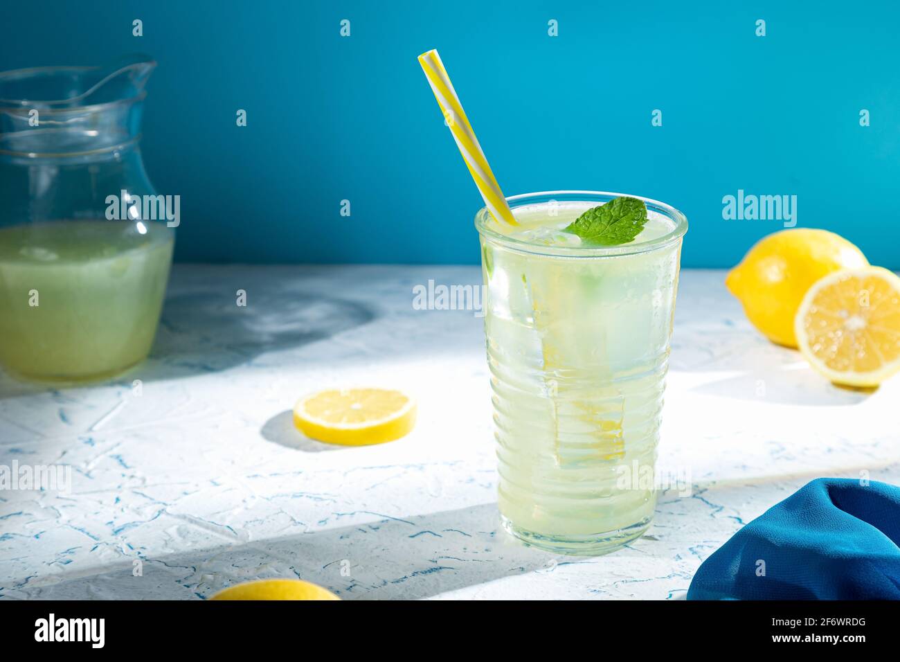 Glass with lemonade and lemons on blue light background Stock Photo - Alamy