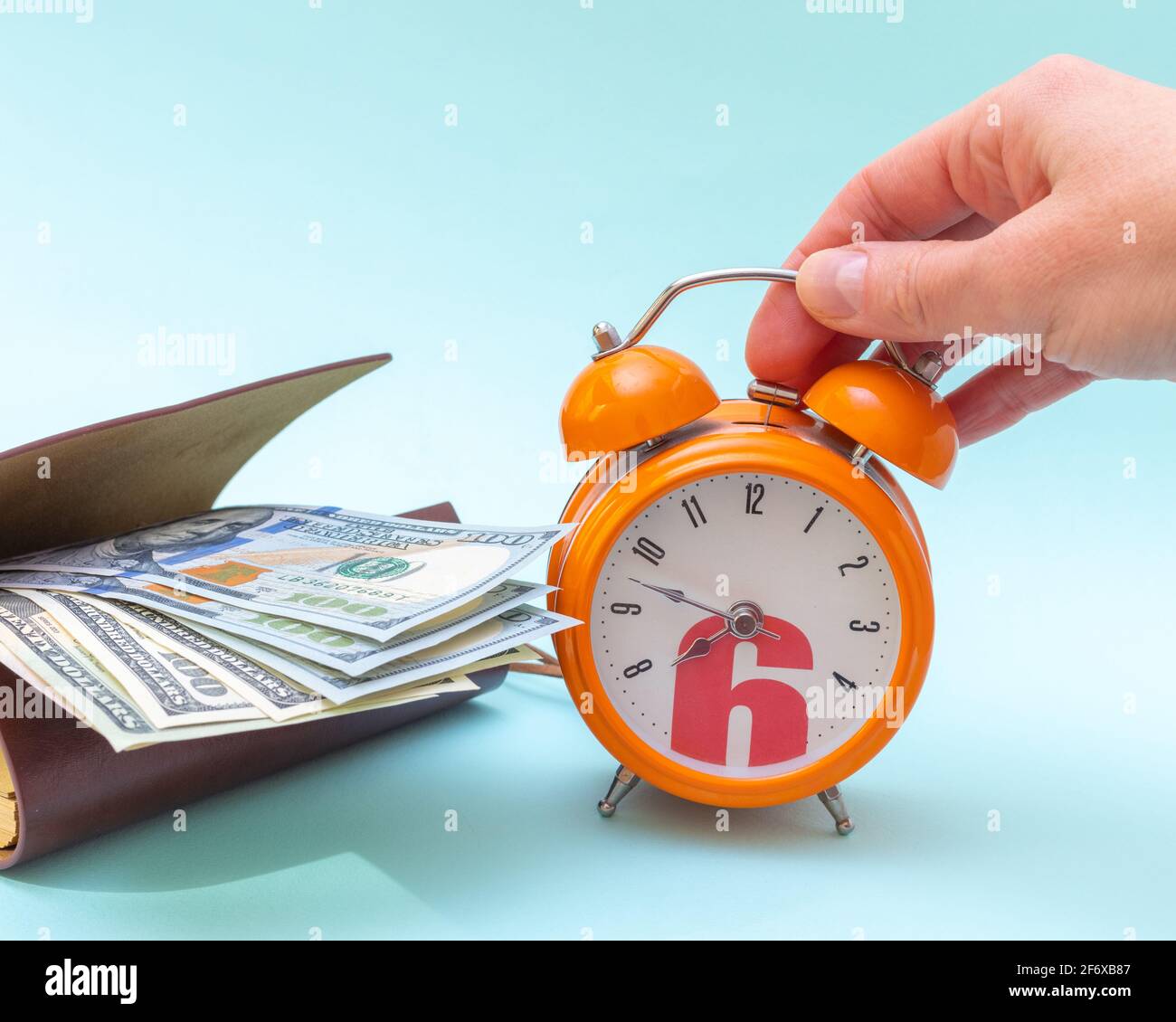Time management concept. A hand holds an orange alarm clock and dollars ...