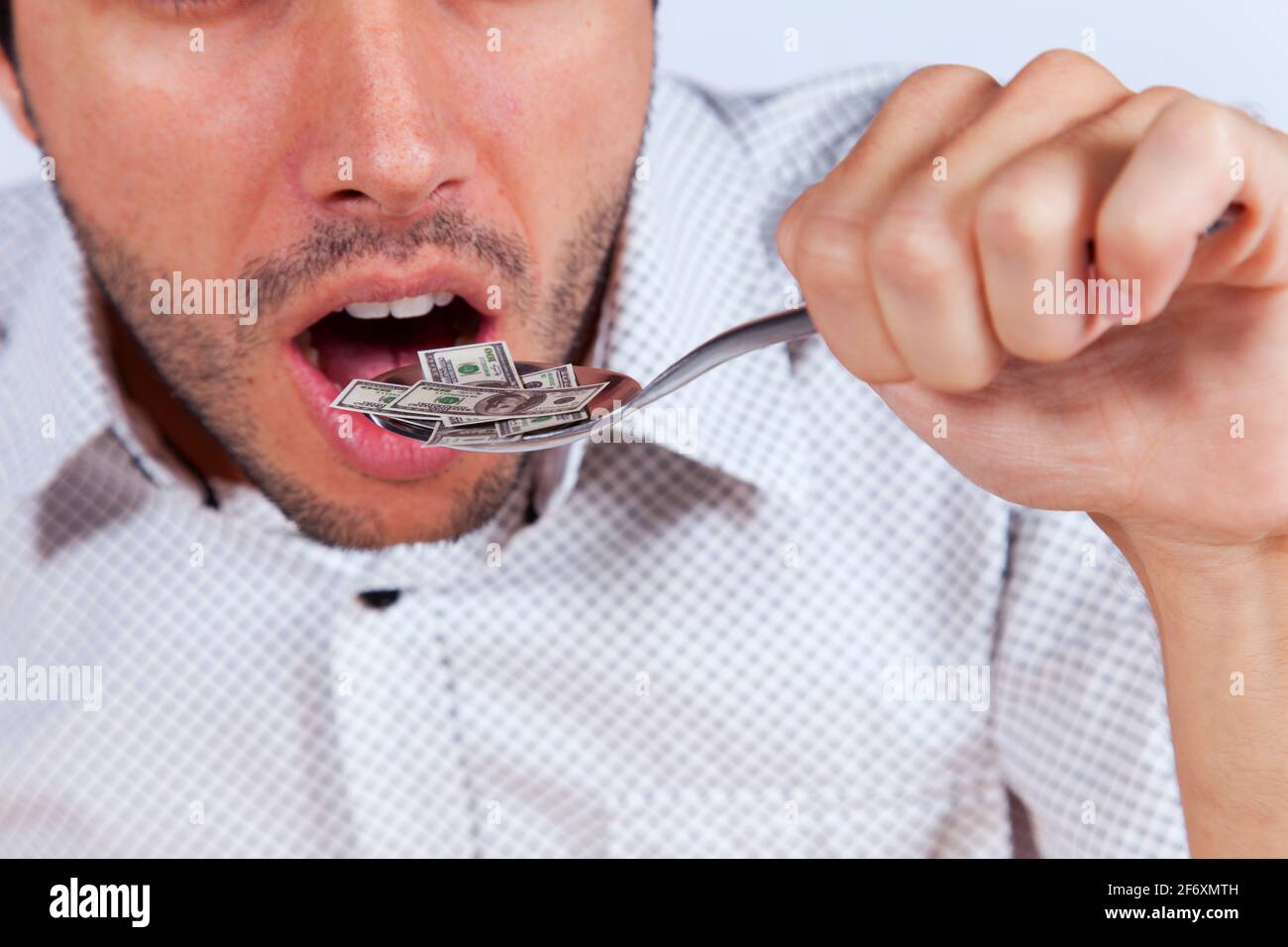 Man eating money at a plate with a fork and a knife Stock Photo - Alamy