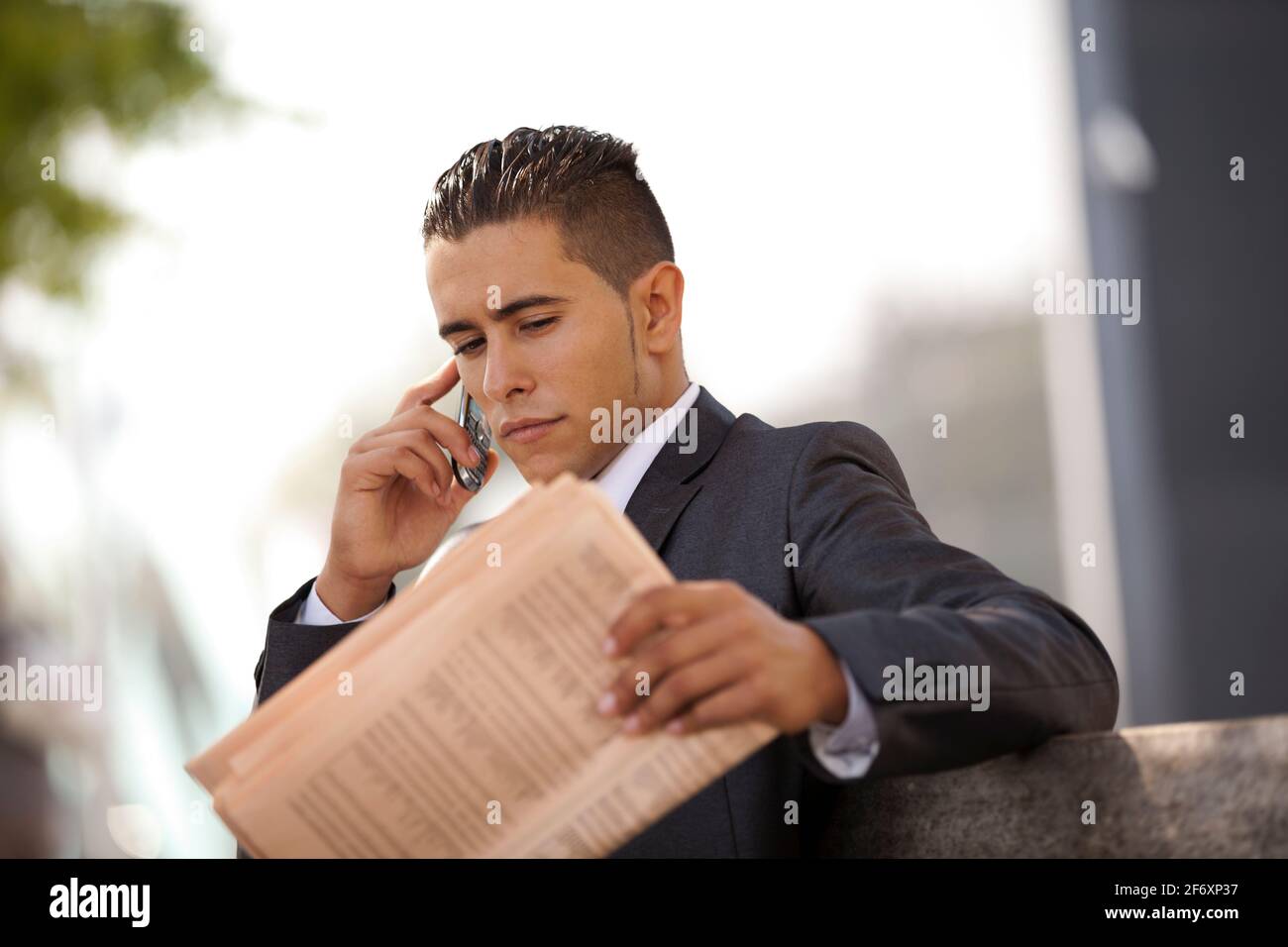 Businessman sited in a bench calling at the cellular and reading his ...