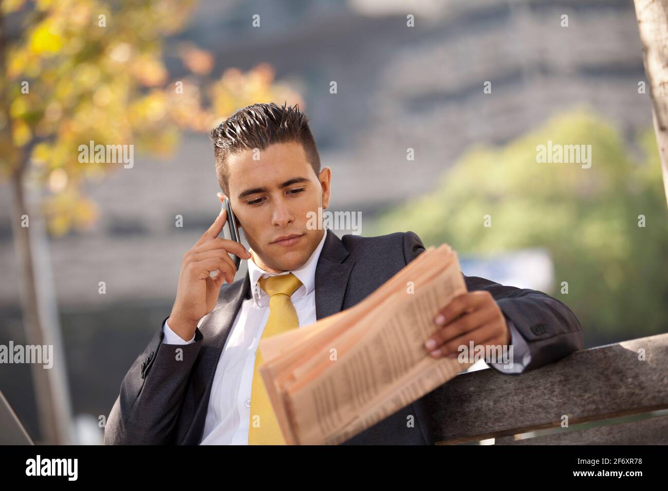 Businessman sited in a bench calling at the cellular and reading his ...