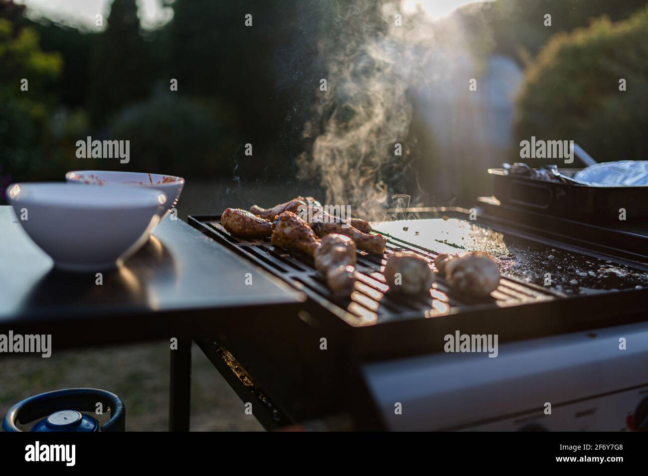Close up of a bbq grill with meats cooking on them, sun flare in the ...