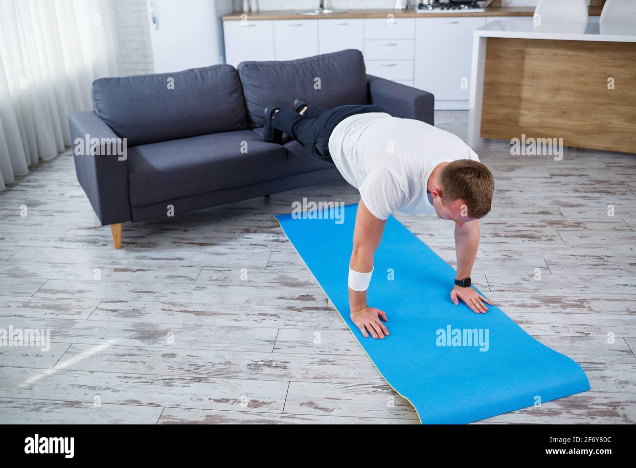 A young man goes in for sports at home, he does push-ups on the couch ...