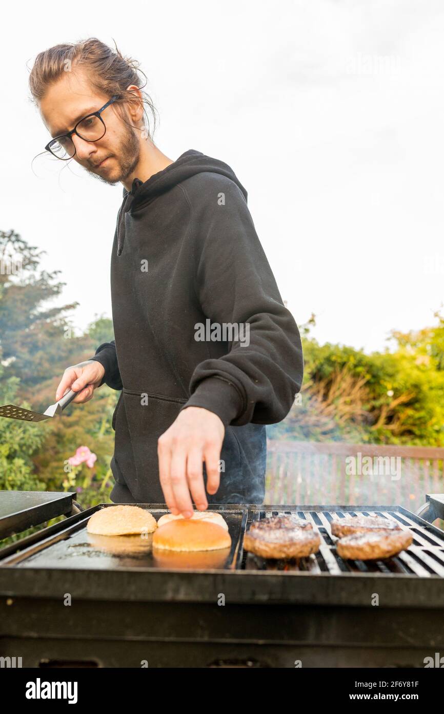 A happy young man cooking meat burgers on barbecue grill - leisure ...