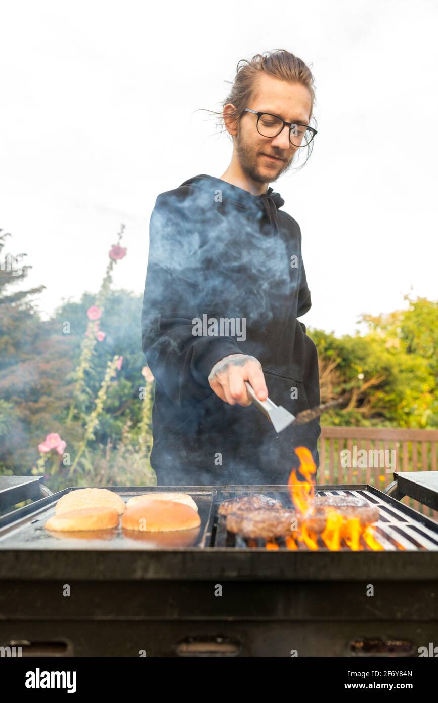 A happy young man cooking meat burgers on barbecue grill - leisure ...