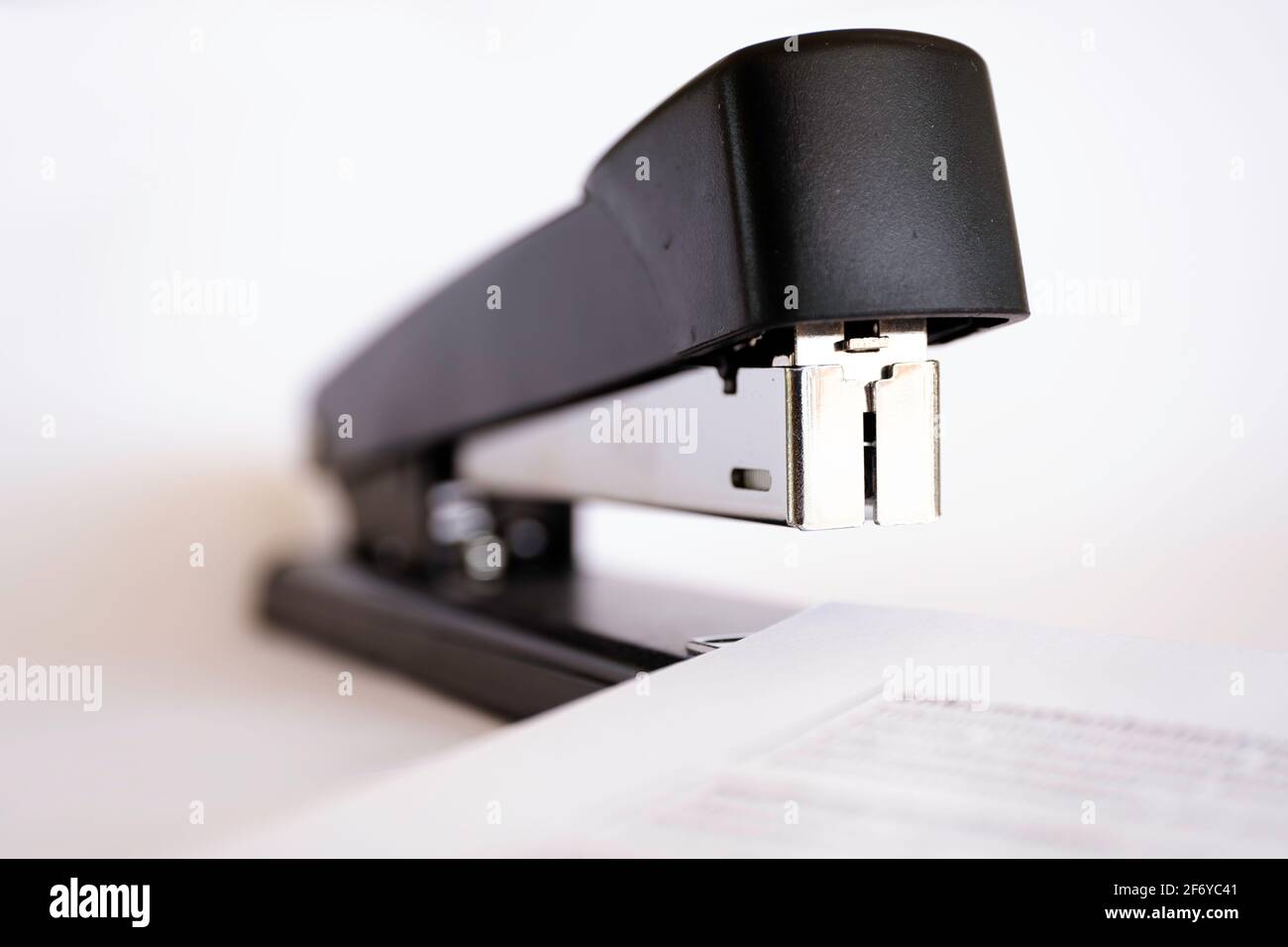 Close-up front view of a black stapler stapling several sheets of paper ...
