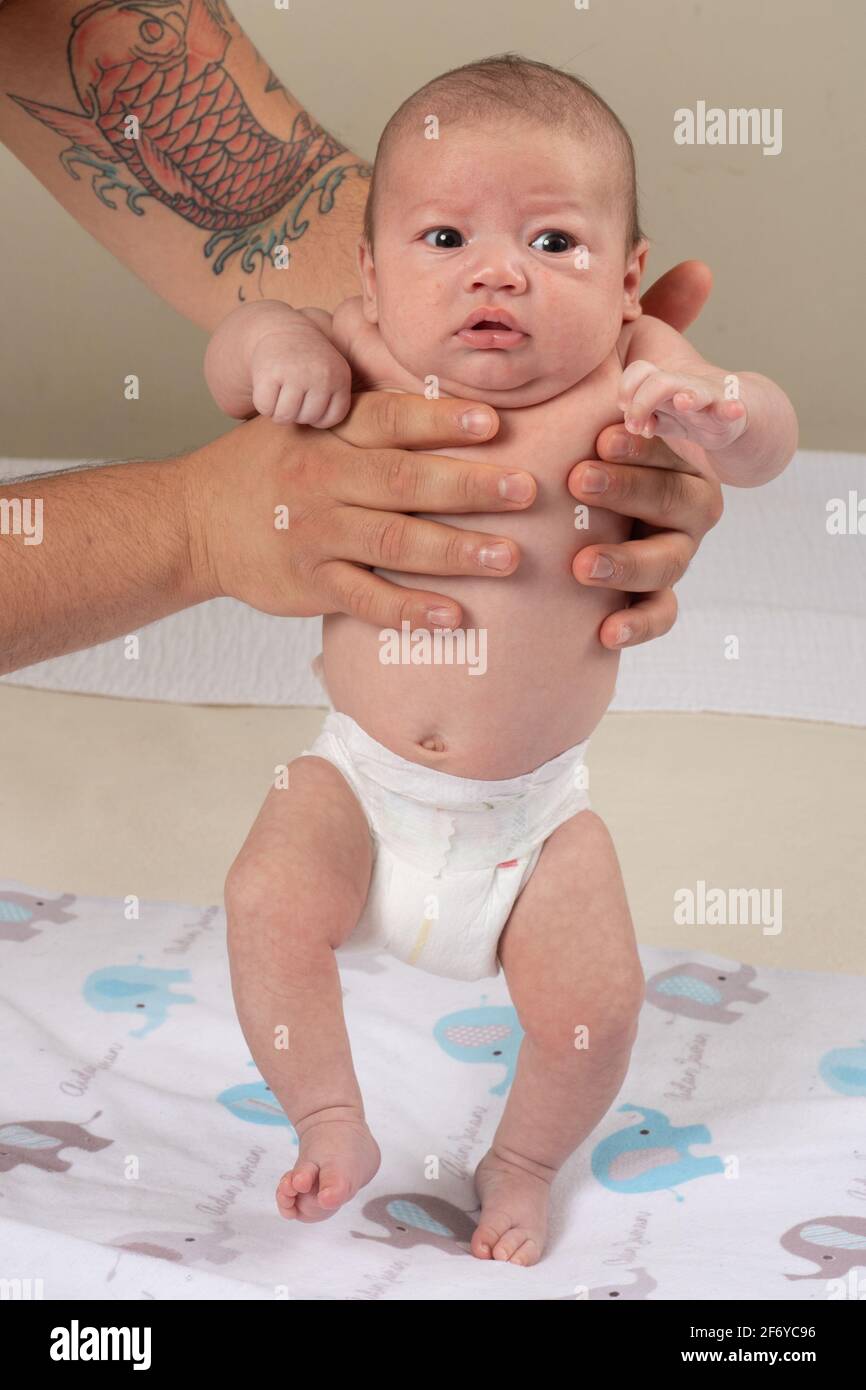 Newborn baby boy 7 weeks old held in standing position with weight on ...