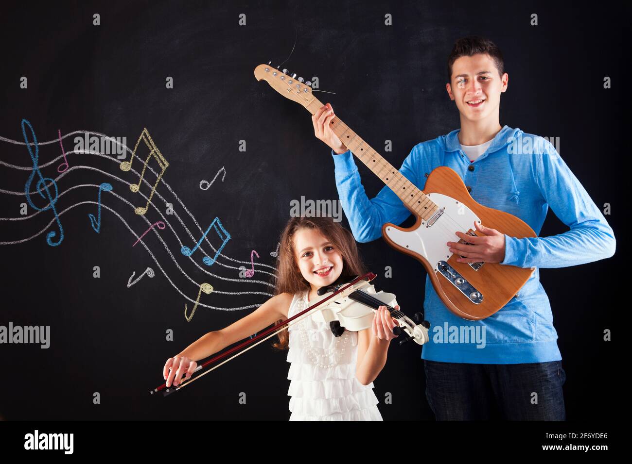 Brother and sister playing a musical instrument next to a blackboard ...