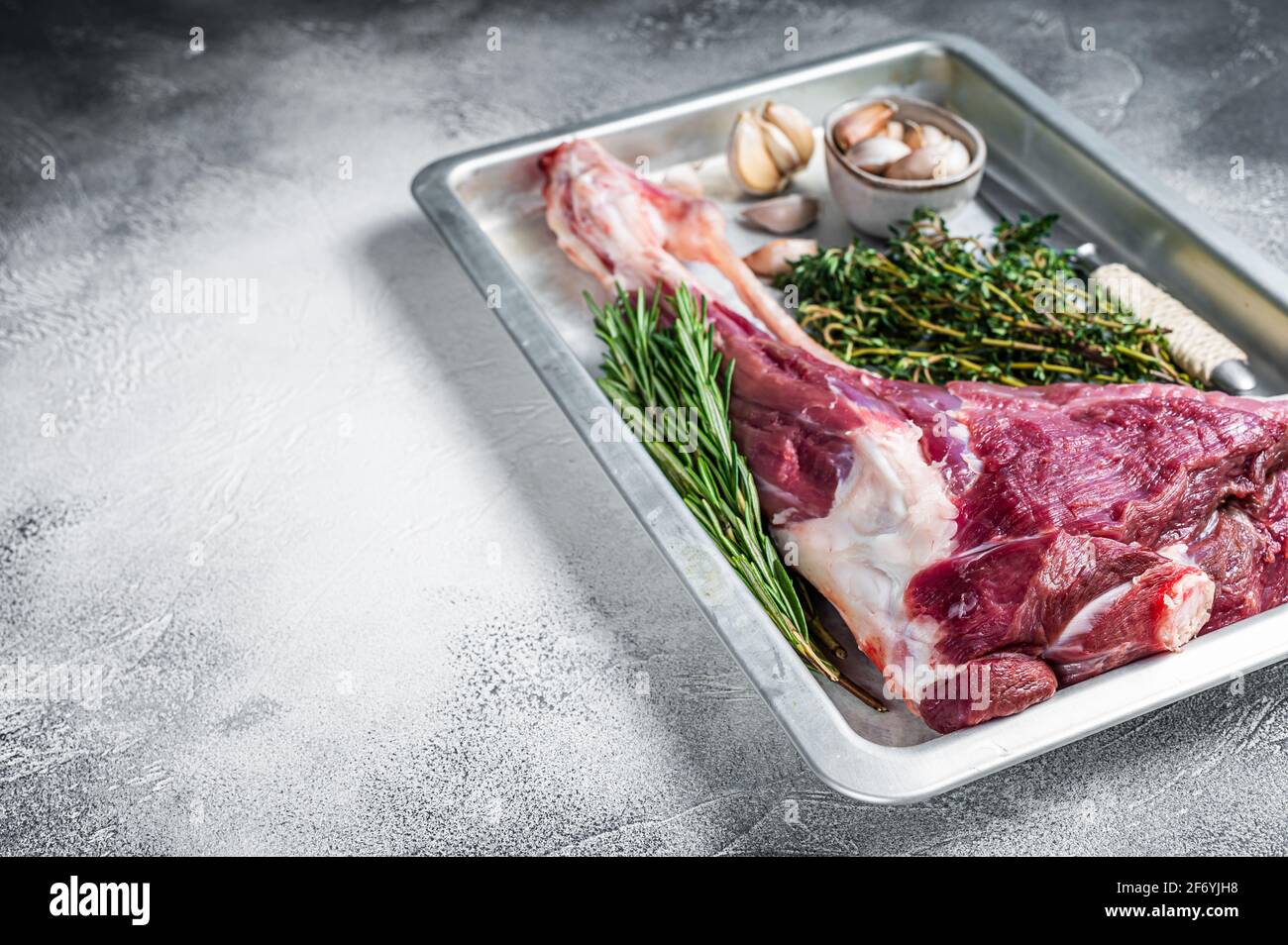 Uncooked Raw goat or lamb leg with herbs in baking tray. White ...