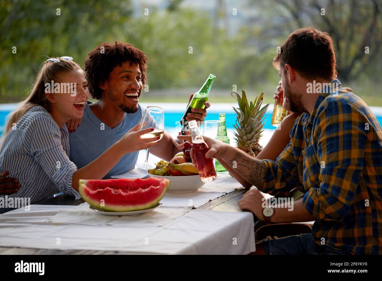 two couples sitting at the table by the pool, talking, smiling ...