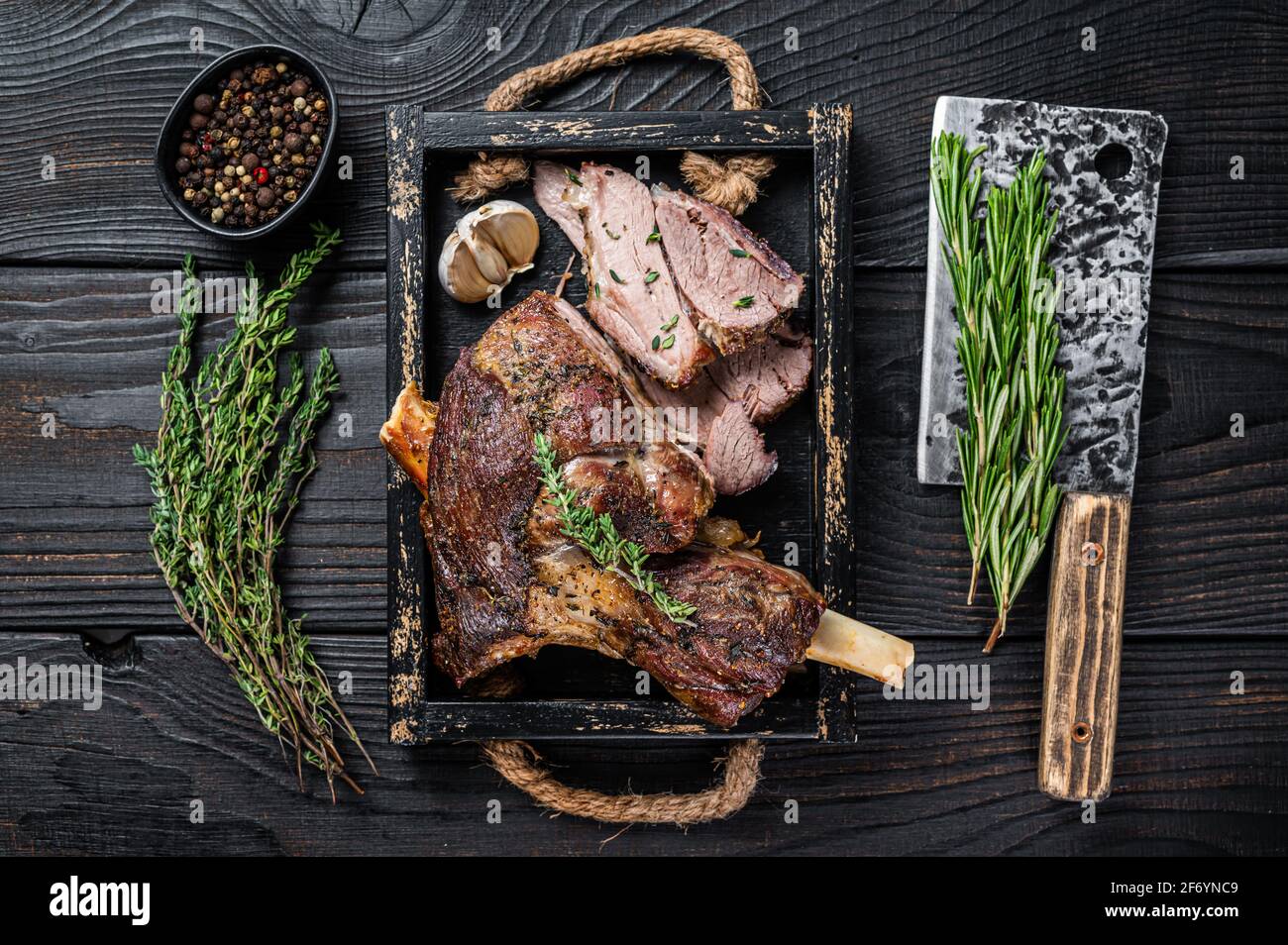 Roasted mutton lamb leg sliced in a wooden tray with meat cleaver ...
