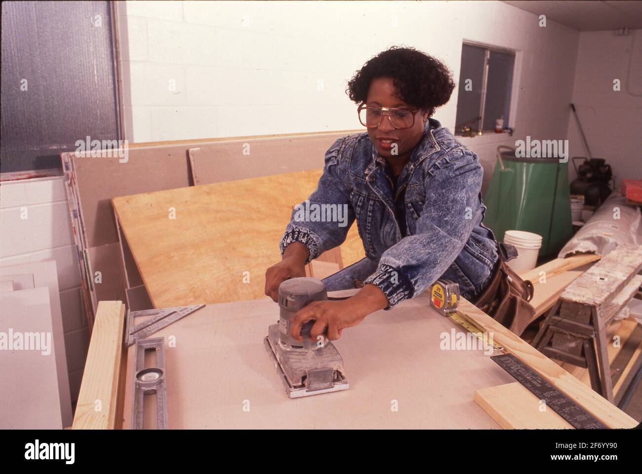 Black female carpenter uses sander on door she built in her workshop ...