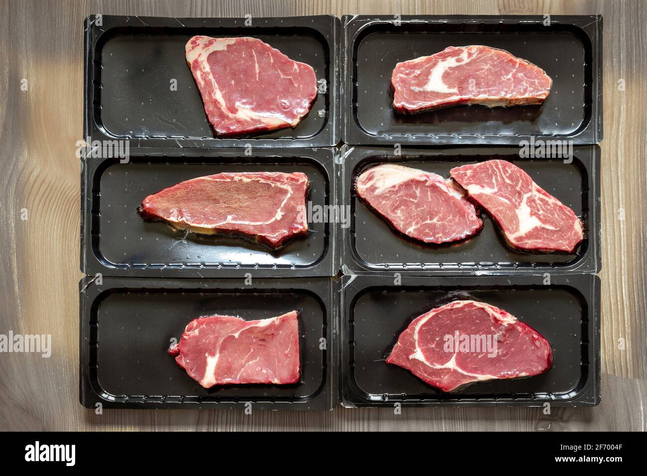 Beef steak in plastic wrap, wooden isolated background Stock Photo - Alamy