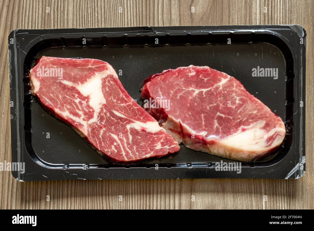 Beef steak in plastic wrap, wooden isolated background Stock Photo - Alamy