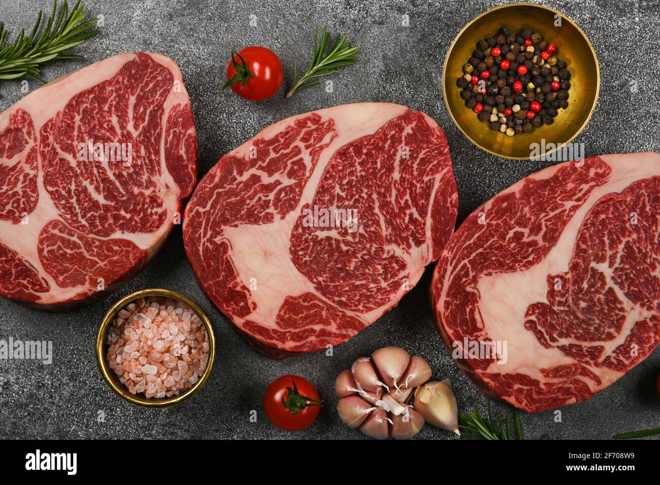 Close up three aged prime marbled raw ribeye beef steaks with spices ...