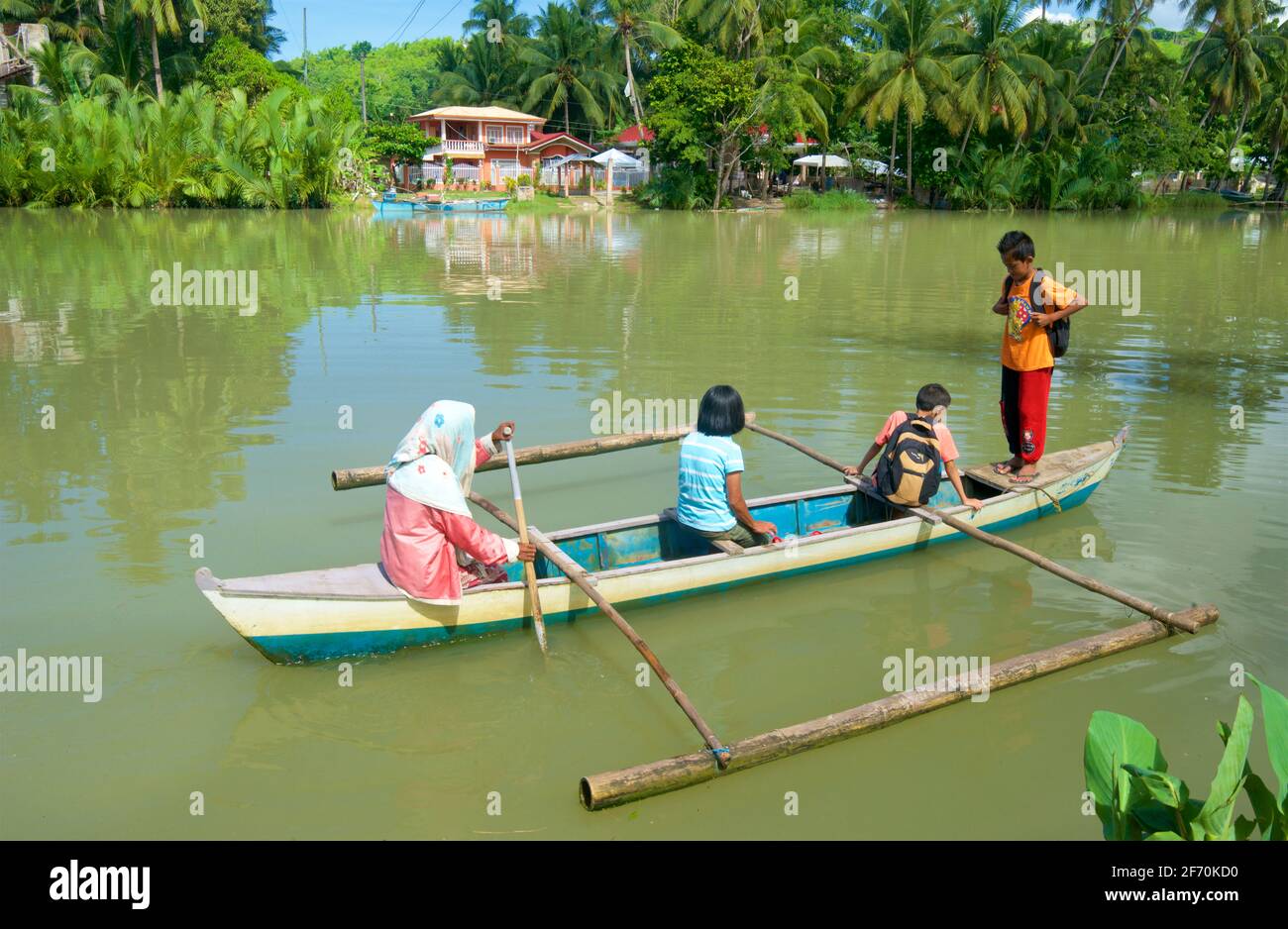 Filipina boatwoman ferrying 3 schooolchildren across the Loboc River in ...