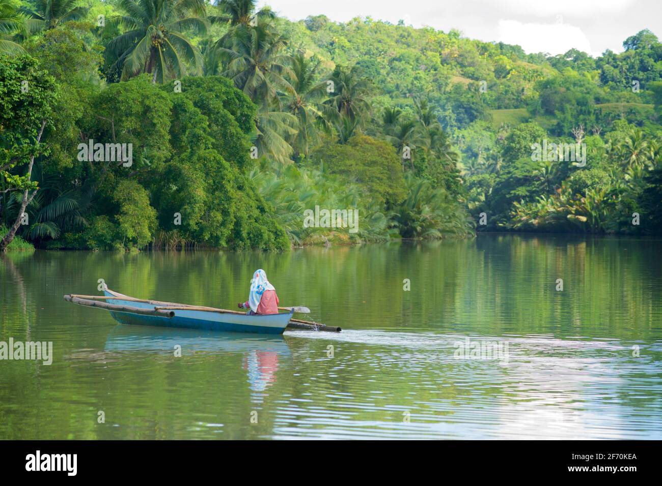 Filipina boatwoman in ther small outrigger canoe crossing the Loboc ...