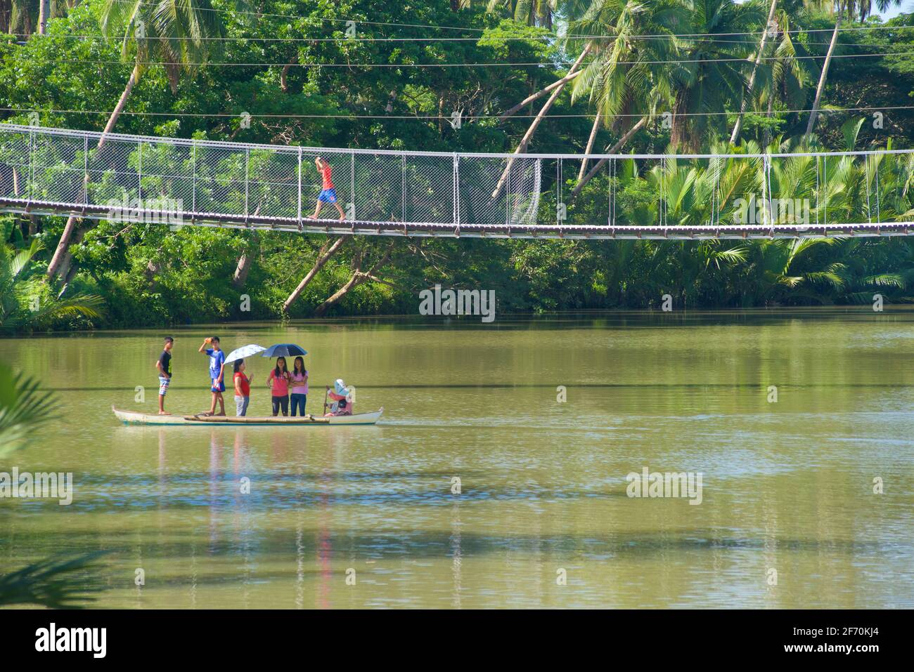 Pedestrian crossing a suspension footbridge over the Loboc River whilst ...