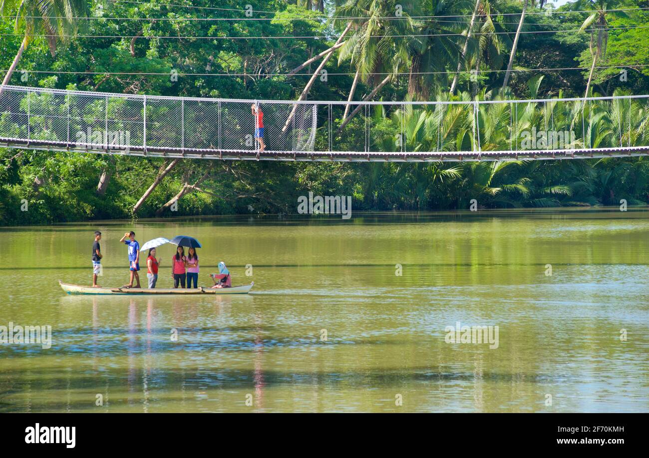 Pedestrian crossing a suspension footbridge over the Loboc River whilst ...