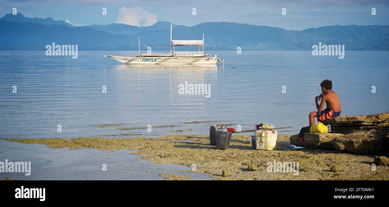 Filipino on a rock at low tide waiting for a boat. Calm morning on the ...