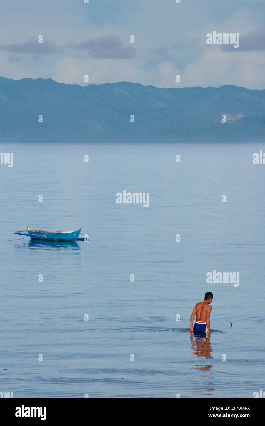 Filipino fisherman heading out to his his small outrigger canoe in the ...