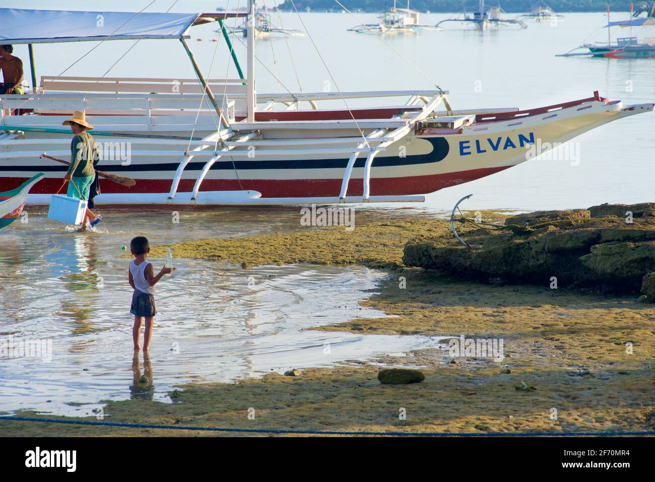 Filipino fisherman iheading out to his boat whilst watched by a boy ...
