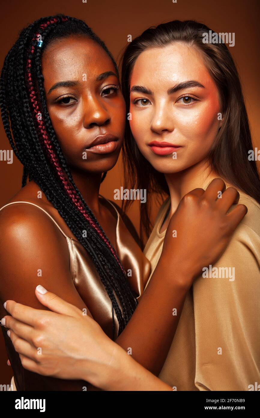 young pretty asian and afro woman posing cheerful together on brown ...